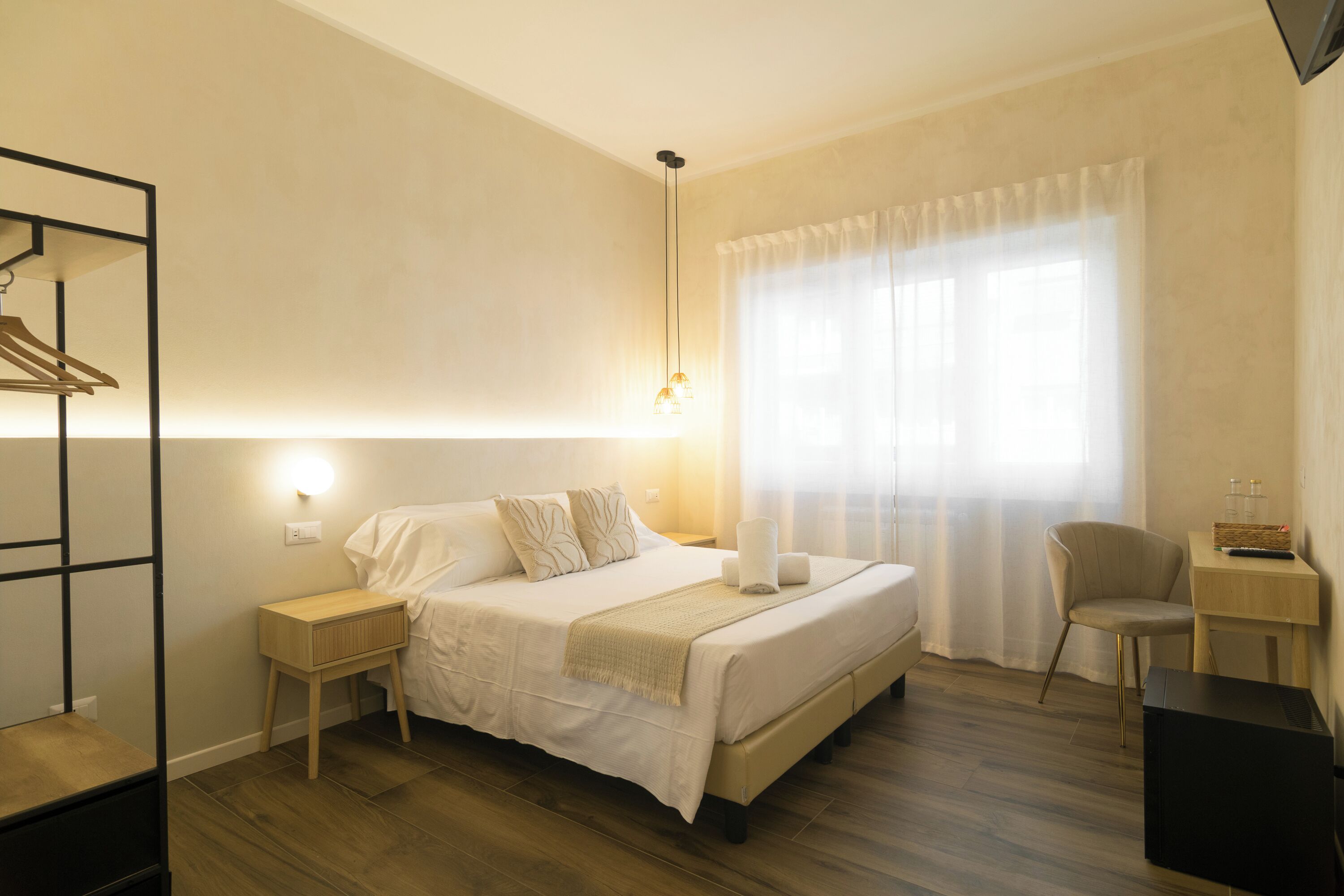 Quarto bem arrumado com cama, mesas de cabeceira, uma cadeira e um suporte para TV.