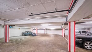 Garagem de estacionamento com vários níveis, pisos de concreto e pilares vermelhos e brancos.