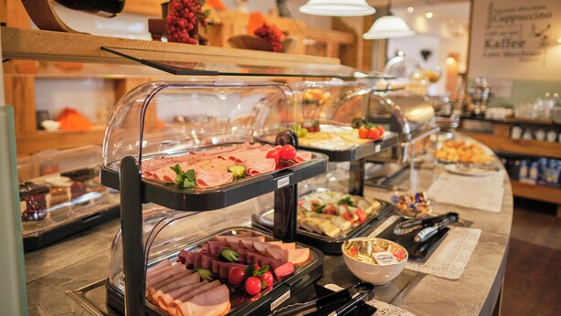 Buffet com diversos alimentos, incluindo carnes e frutas, expostos em recipientes transparentes.