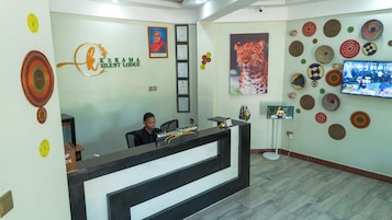 Balcão de recepção com um homem sentado atrás, cercado por várias decorações de parede, incluindo padrões circulares e um certificado emoldurado.