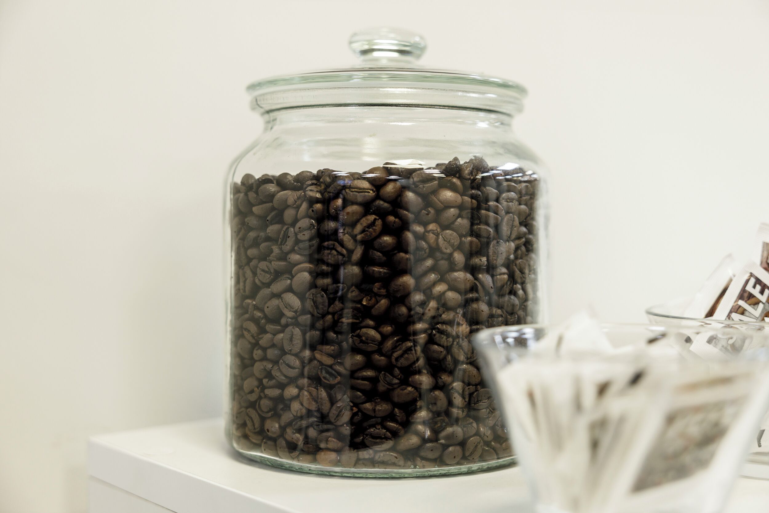 Um frasco de vidro cheio de grãos de café sobre uma superfície branca.