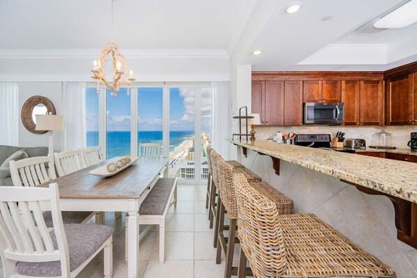 Uma sala de jantar com vista para o oceano, uma cozinha com armários de madeira e um espaço de bar com bancos de vime.