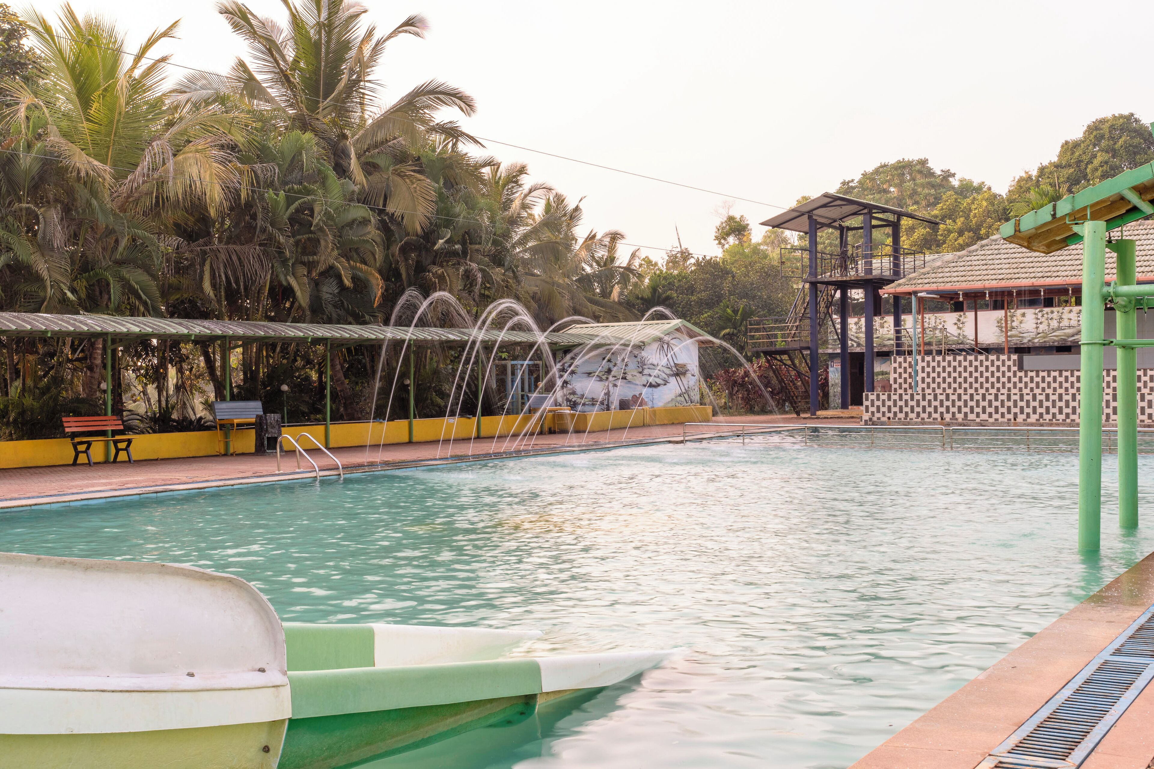 Uma piscina com uma fonte de água, cercada por palmeiras e uma área de estar coberta.