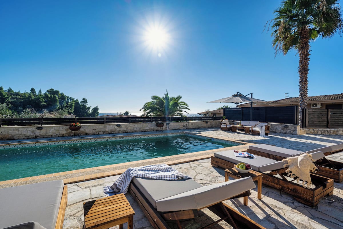 Uma área à beira da piscina com espreguiçadeiras, um deck de pedra e vista para a piscina.