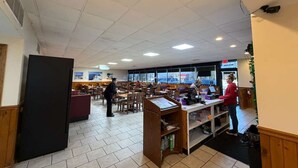 Um espaço amplo e interno com várias mesas e cadeiras, um balcão e uma tela grande.