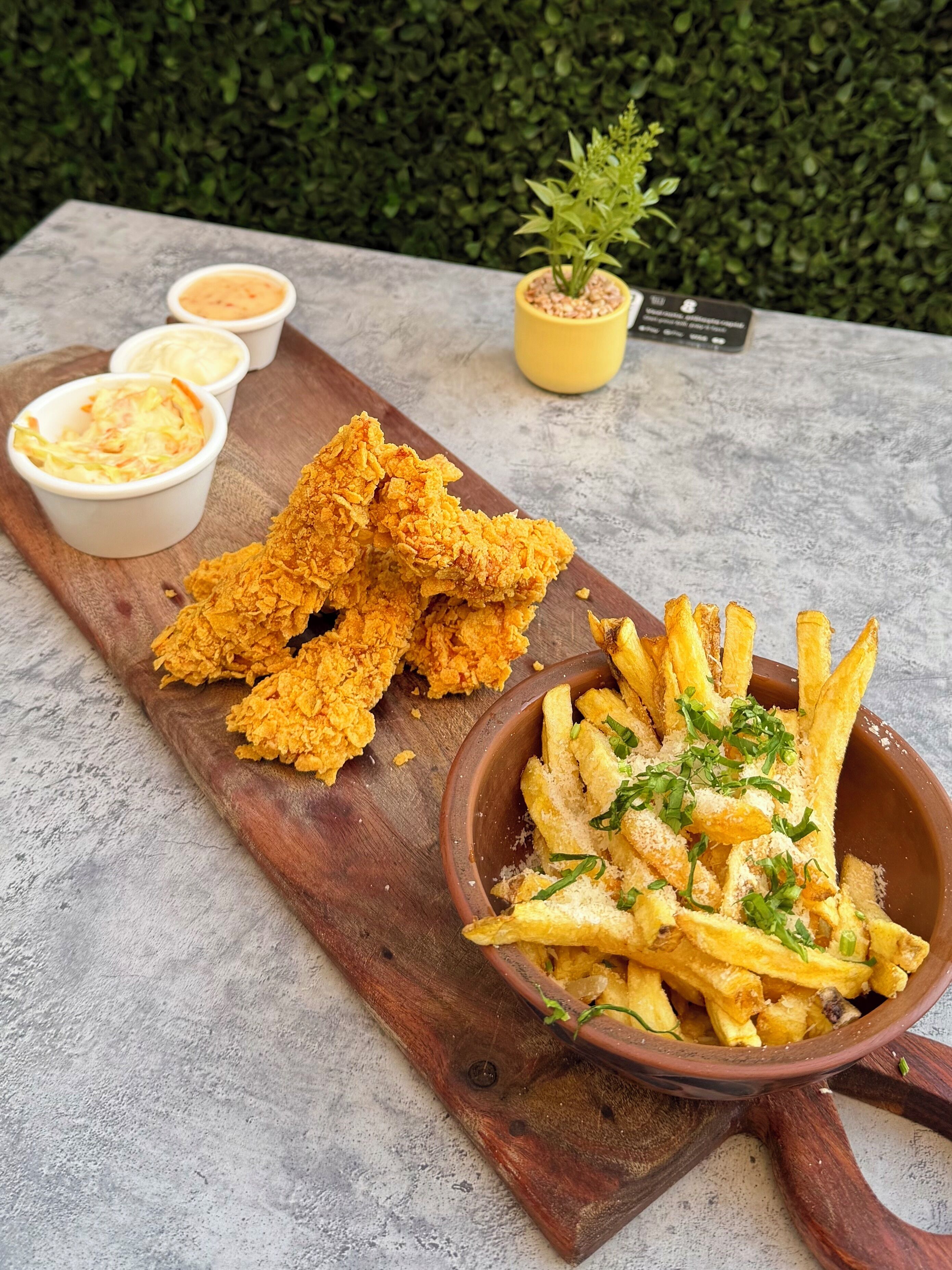Uma mesa com frango frito e batatas fritas, acompanhadas de molhos para acompanhar.