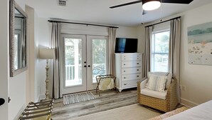 Quarto com ventilador de teto, televisão em uma cômoda, uma cadeira de vime e uma cama.
