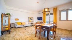 Uma área de refeições com uma mesa e cadeiras de madeira, um sofá, uma televisão e uma janela com cortinas amarelas.