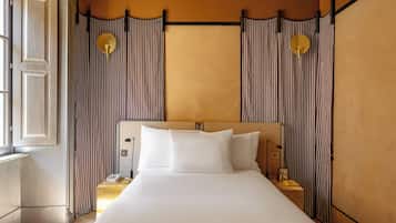 Quarto de hotel com uma cama grande, cortinas listradas, mesa de cabeceira com abajur e janela.