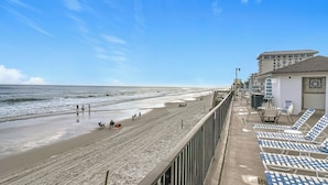 Vista da praia com calçadão, cadeiras de praia e um prédio com um relógio.
