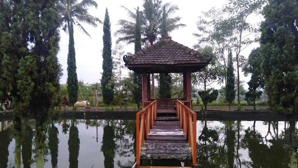 Um gazebo com uma escadaria de madeira que leva a ele, cercado por água e árvores.