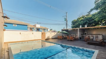 Piscina com deck de madeira, área de estar externa e vista para edifícios próximos.