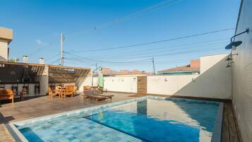 Piscina no terraço com espreguiçadeiras de madeira e área para churrasco.