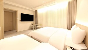 Quarto de hotel com uma cama grande, televisão na parede, uma mesinha com duas cadeiras e uma porta para outro quarto.