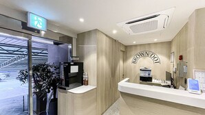 Uma área de recepção moderna com uma máquina de café, uma lixeira e uma placa com a inscrição "BROWN DOT".