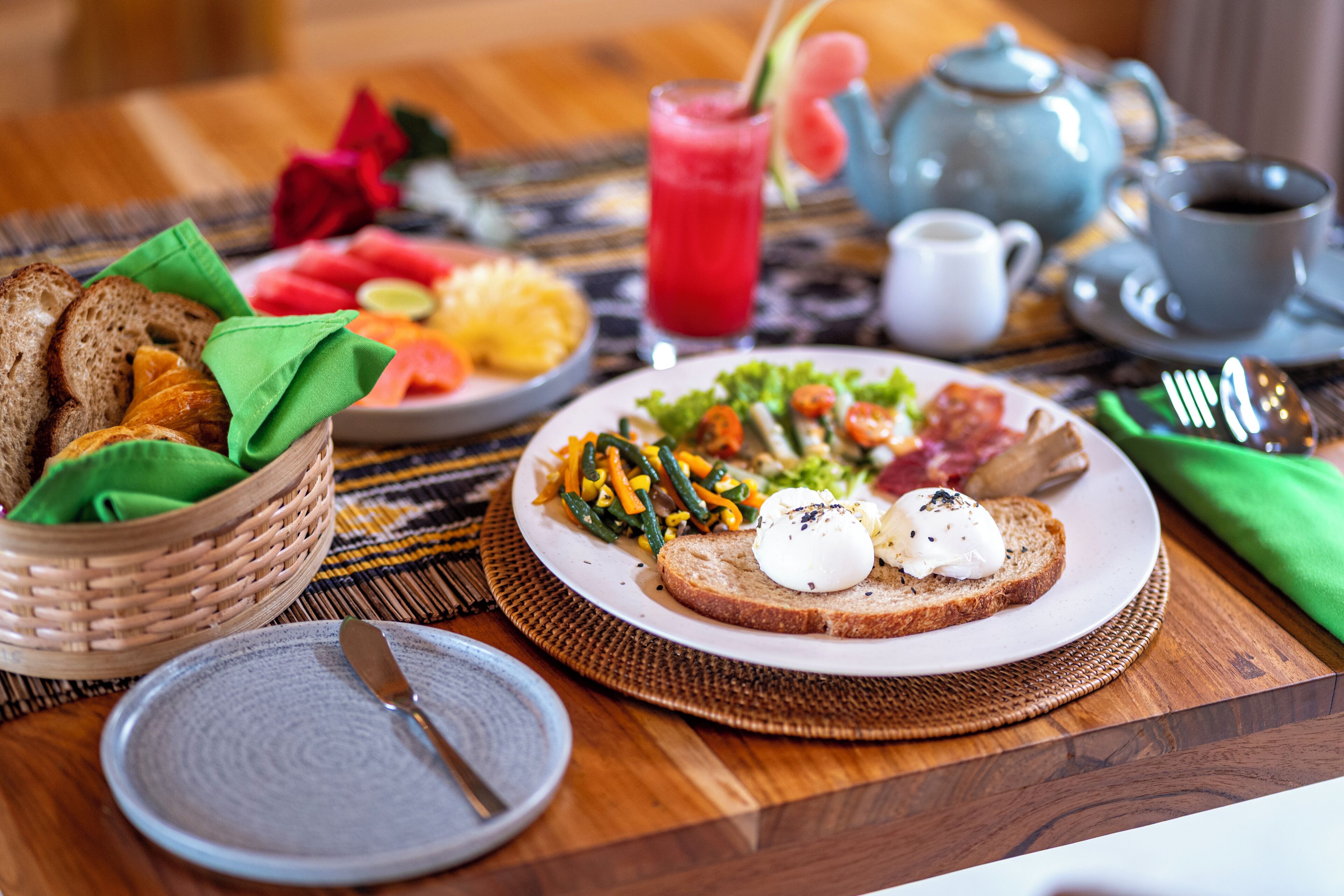 Uma mesa de café da manhã com torradas, ovos, legumes e uma cesta de frutas.