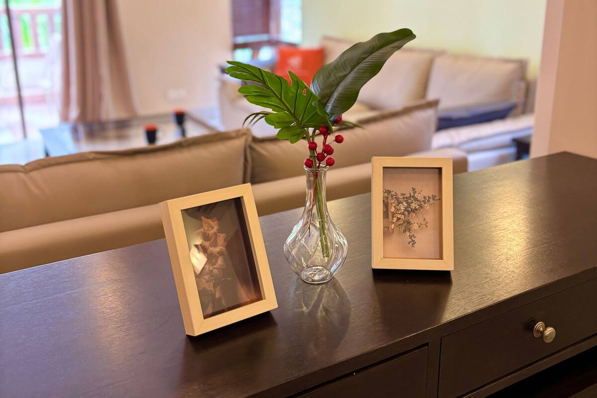 Uma sala de estar moderna com um armário de madeira escura, um vaso de vidro com berris vermelhas e duas fotos emolduradas no armário.