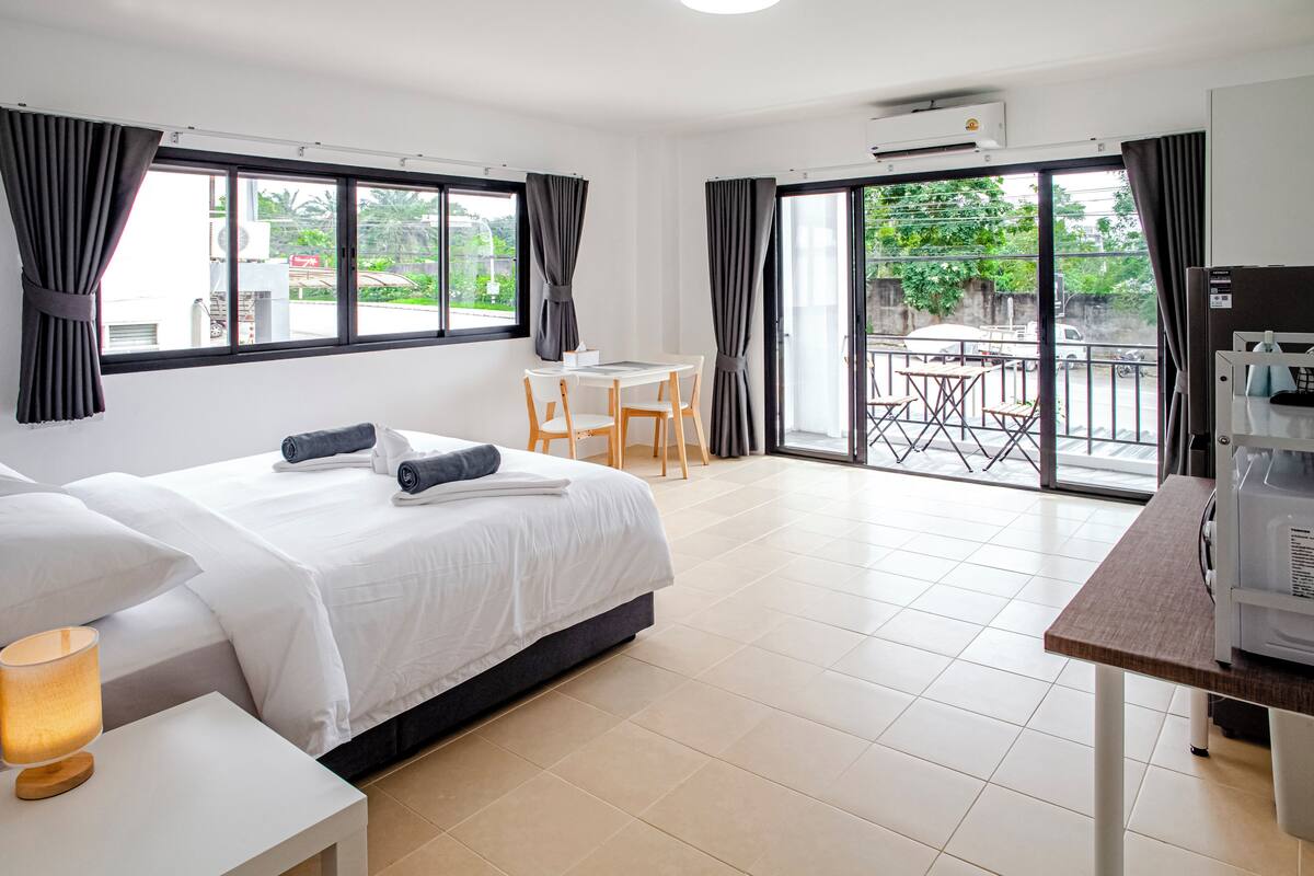 Quarto de hotel com cama, escrivaninha, cadeira e varanda com mesa e cadeiras.