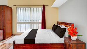 Quarto com cama, guarda-roupa de madeira, janela com persianas e mesa de cabeceira com um vaso de flores.