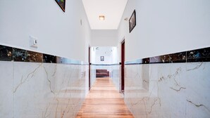 Um corredor com paredes de mármore e chão de madeira, que leva a um quarto com sofá vermelho.