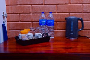 Uma mesa com uma bandeja preta contendo uma garrafa de água, um termo e uma caneca. Há duas garrafas de água e uma chaleira sobre a mesa.