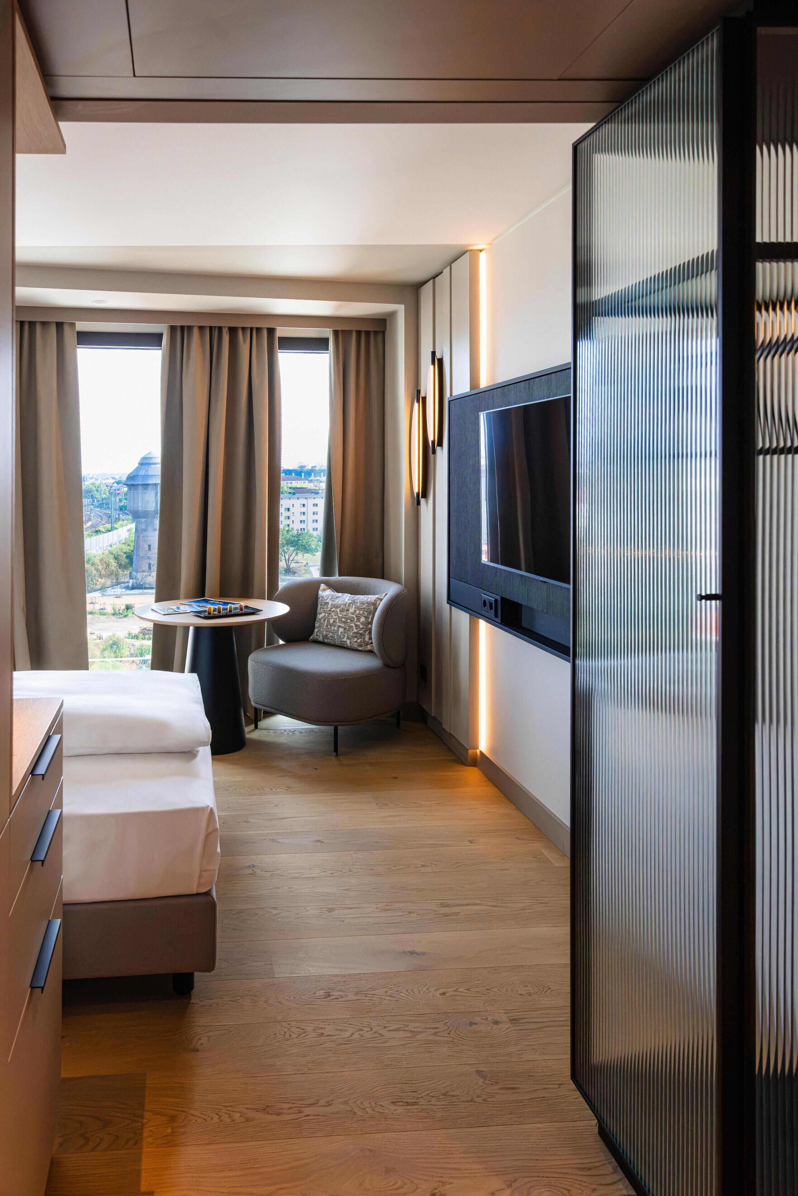 Quarto de hotel com cama, escrivaninha, cadeira, televisão e vista para a cidade.