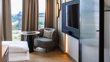 Quarto de hotel com cama, escrivaninha, cadeira, televisão e vista para a cidade.