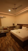 Quarto de hotel com cama, sofá, mesa de centro, ventilador de teto e ar condicionado.
