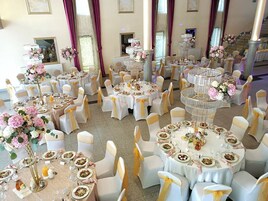 Uma sala de banquetes com mesas redondas, cadeiras brancas e centros de mesa florais.