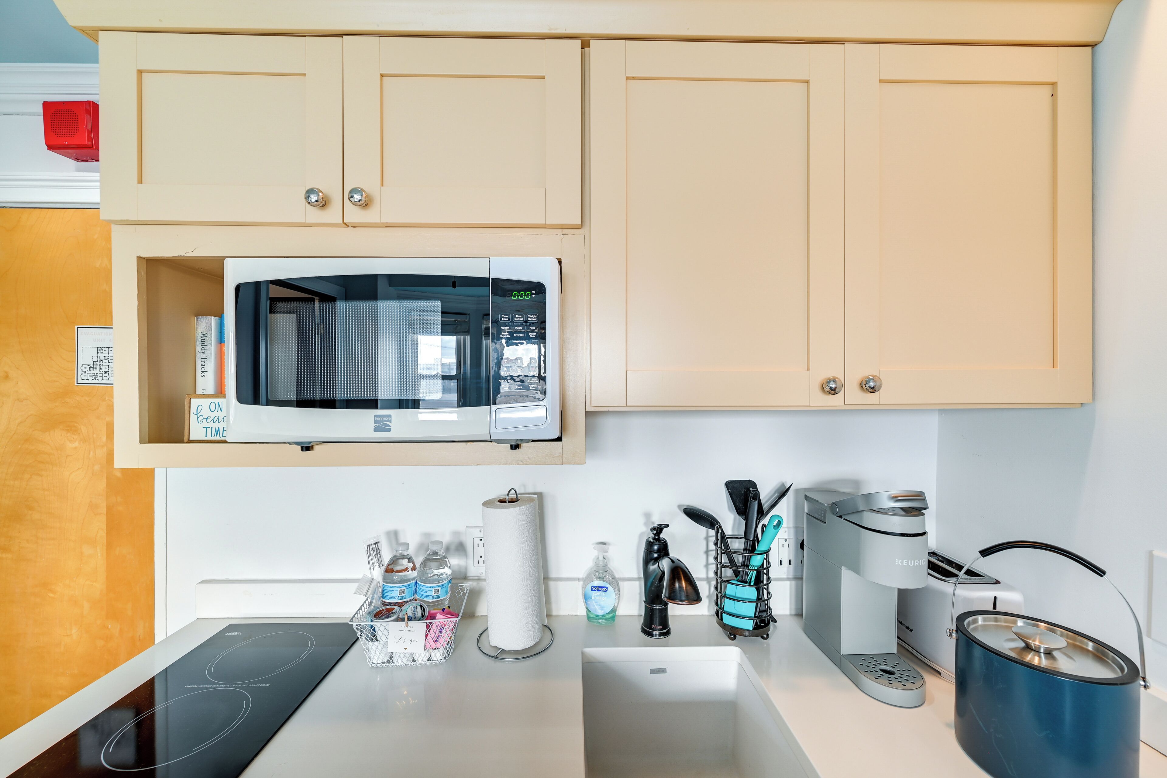 Uma cozinha moderna com micro-ondas integrado, máquina de café, torradeira e chaleira.