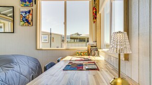 Um quarto com uma janela grande, uma mesa de madeira com uma luminária e obras de arte na parede.