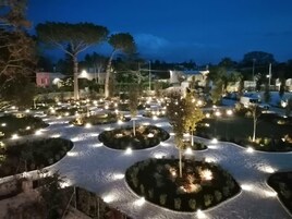 Uma área de jardim ajardinada com caminhos e árvores, iluminada por luzes no chão.