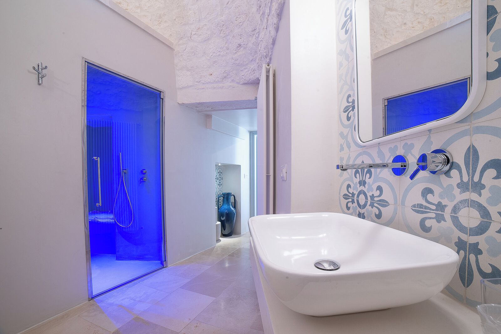 Um banheiro moderno com uma pia grande e branca, um chuveiro com iluminação azul e azulejos decorativos nas paredes.
