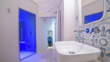 Um banheiro moderno com uma pia grande e branca, um chuveiro com iluminação azul e azulejos decorativos nas paredes.