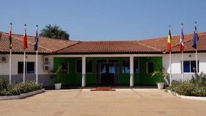 Um edifício com fachada verde e telhado telhado, cercado por vasos de plantas e várias bandeiras.