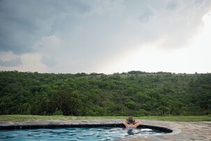 Uma pessoa relaxando em uma piscina, com uma encosta verdejante ao fundo.
