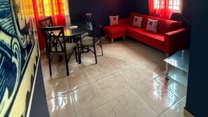 Uma sala de estar com um sofá vermelho, uma mesa de jantar com cadeiras e um ventilador de teto.