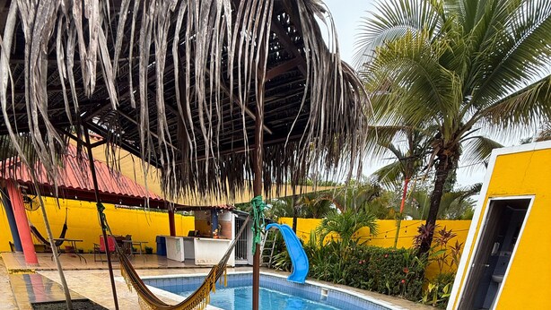 Piscina com escorregador, rodeada por plantas tropicais e uma estrutura de telhado de palha.