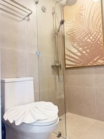 Um banheiro moderno com vaso sanitário, box de vidro para chuveiro e porta-toalhas fixado na parede.