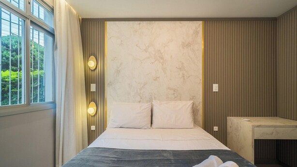 Quarto de hotel com cama, mesa de cabeceira, espelho e janela com cortinas.