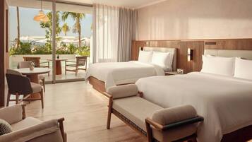 Quarto de hotel com duas camas, área de estar com mesa e cadeiras, e vista para o oceano.