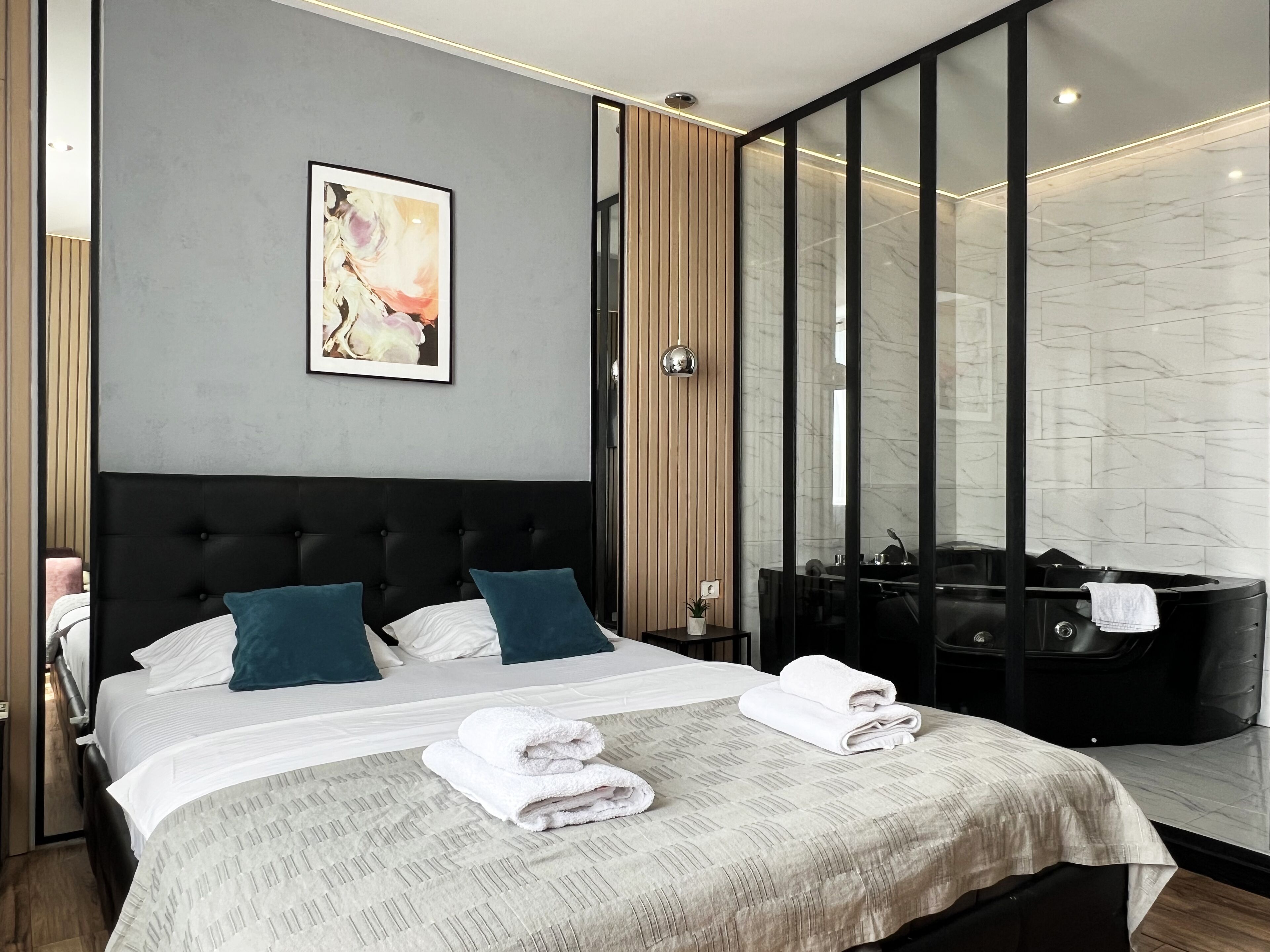 Quarto de hotel moderno com uma cama grande, divisória de vidro, banheira e um quadro na parede.