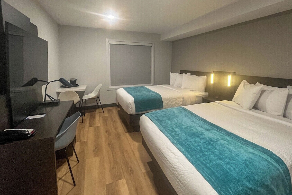 Quarto de hotel com duas camas, uma escrivaninha e uma cadeira.