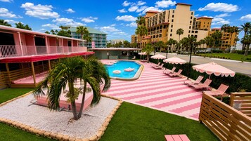 Uma área de piscina com piso xadrez rosa e branco, cadeiras de descanso e piscina com boias.