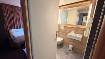 Quarto de hotel com cama, banheiro com pia, vaso sanitário e espelho.