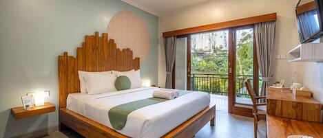 Um quarto espaçoso com uma cama de madeira, mesa de cabeceira, escrivaninha com cadeira e uma grande janela com vista para o verde.