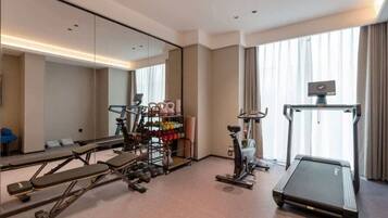 Quarto de hotel com área de ginásio, incluindo esteiras, pesos e equipamentos de exercício.