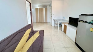Uma sala de estar moderna com sofá, mesa de jantar e cozinha equipada, incluindo frigorífico e televisão.
