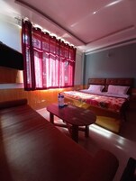 Quarto de hotel com cama, sofá, mesinha com uma garrafa de água e televisão na parede.