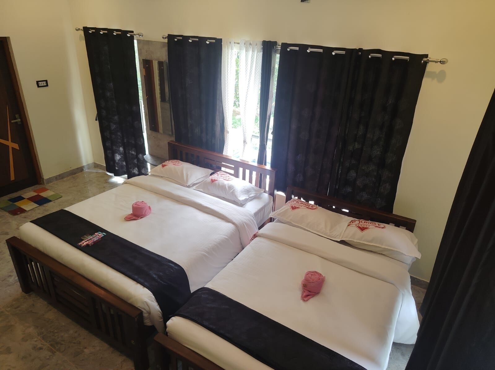 Quarto de hotel com duas camas de solteiro, cabeceira de madeira, pequena janela com cortinas e chão de azulejos.